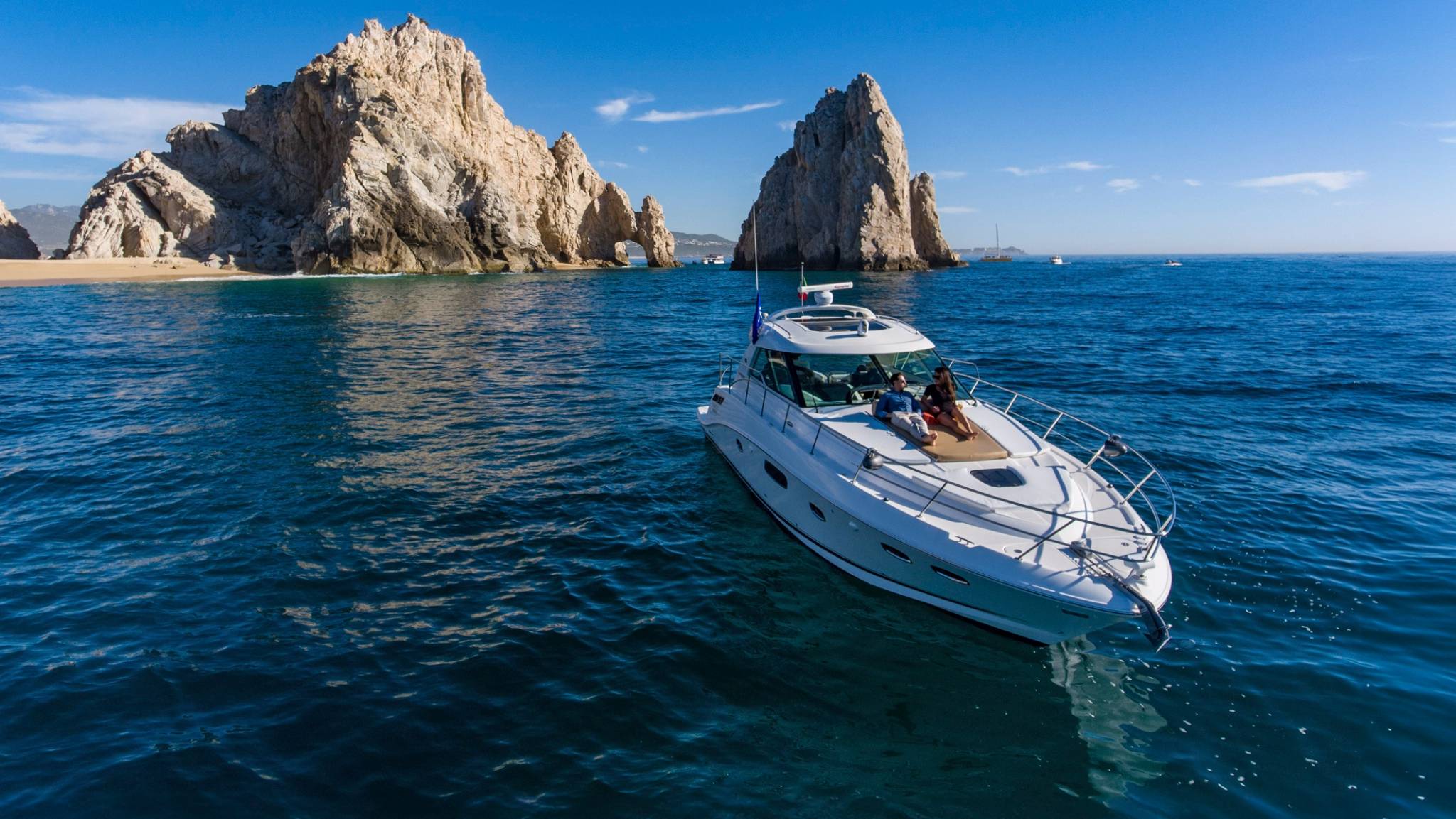 A luxury yacht cruises by the rock formations of Los Cabos under a ...