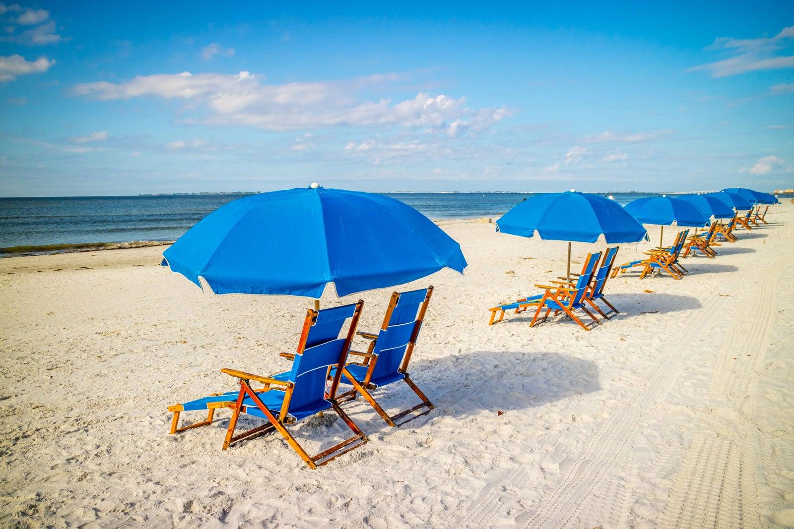 Row of blue sun umbrellas and deck chairs on a beach.