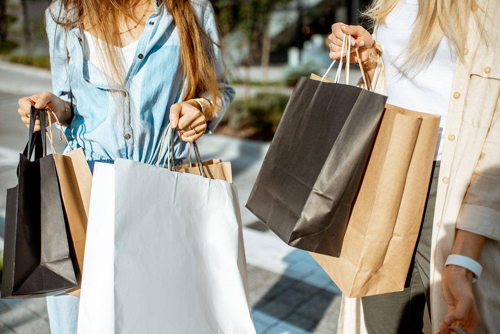 Women holding shopping bags outdoors while shopping, close-up view on the empty paper bags with copy space