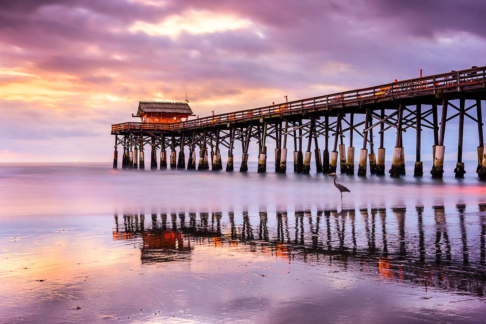 Long pier, a bird by water, sunshine through clouds.