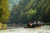 People float on a traditional wood raft on a river with mountain greenery.